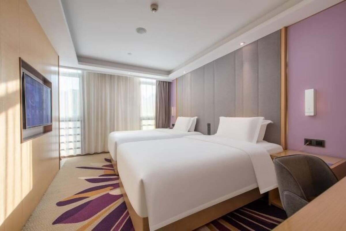 Quarto de hotel com duas camas, televisão, escrivaninha e janela com cortinas.