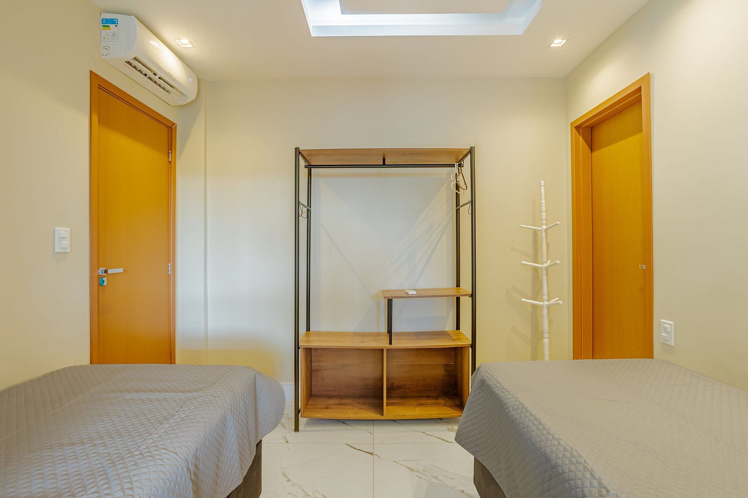 Quarto com duas camas, guarda-roupa, cabideiro e ar condicionado.