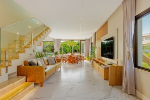 Uma sala de estar moderna com sofá, mesa de jantar e televisão. Uma escada leva a um andar superior.
