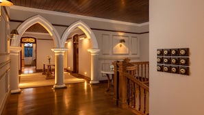 Um corredor com piso de madeira, colunas brancas e escada de madeira.