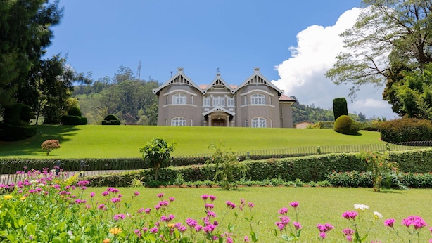 Um edifício grande e imponente, com fachada simétrica, rodeado por jardins bem cuidados e canteiros de flores vibrantes.