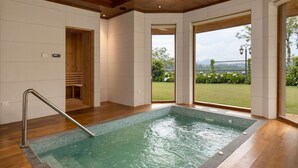 Área de spa com teto de madeira, piscina interior pequena e vista para um jardim através de grandes portas de vidro.