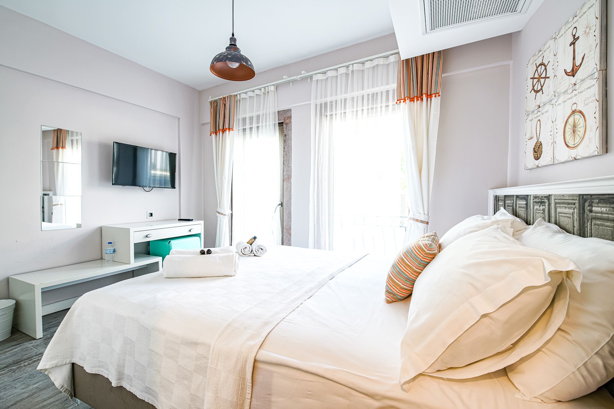 Quarto moderno com uma cama grande, uma televisão, uma toucador e uma janela com cortinas.