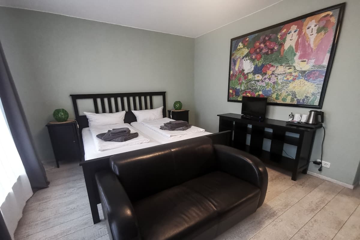Um quarto com uma cama, um sofá de couro preto, uma televisão e um quadro na parede.
