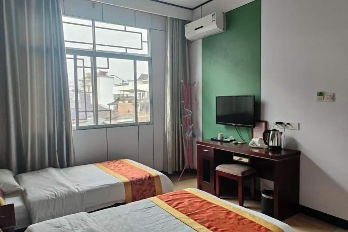 Quarto de hotel com duas camas, uma mesa com cadeira, televisão e ar condicionado.