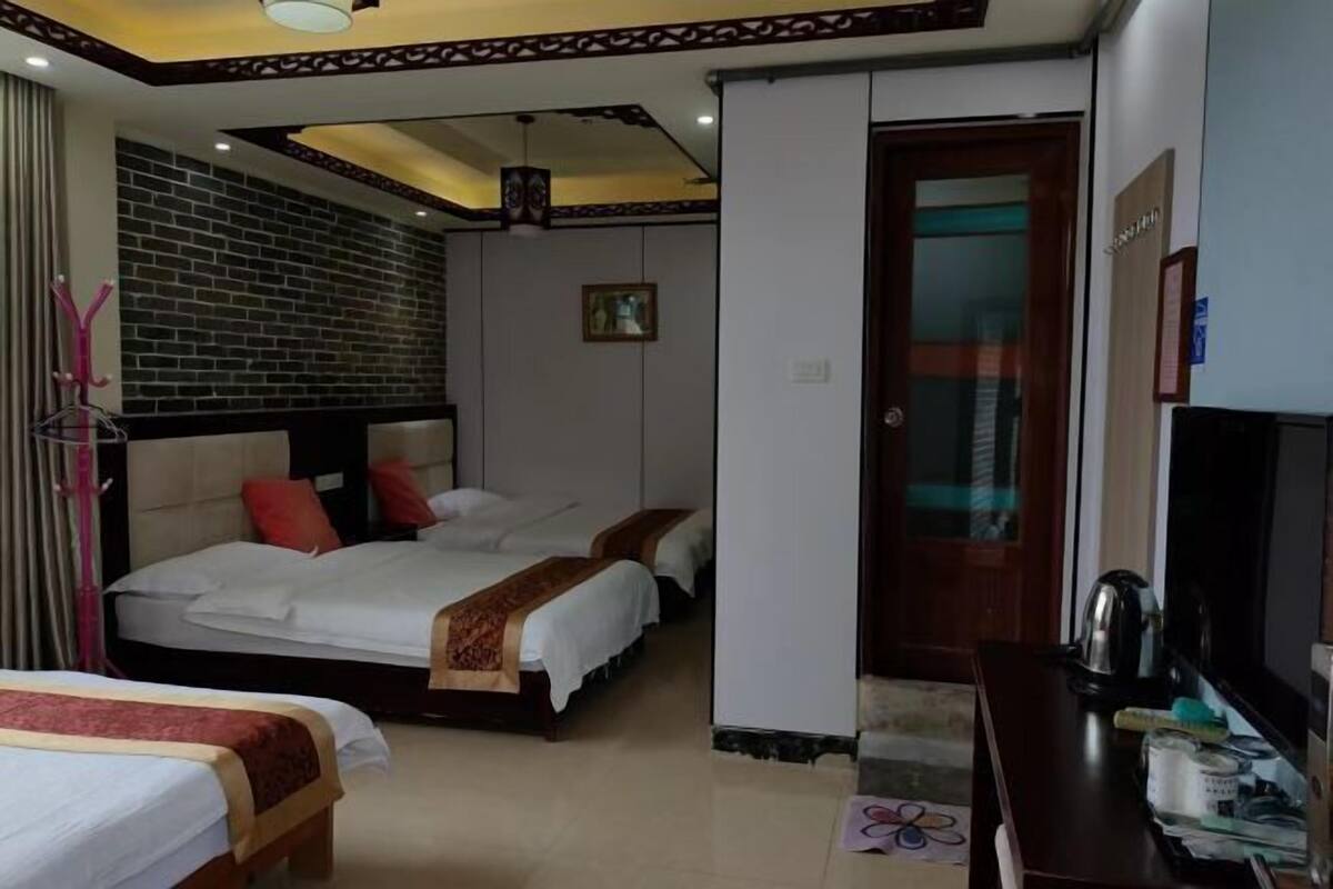 Quarto de hotel com duas camas, televisão, escrivaninha e parede de tijolos.