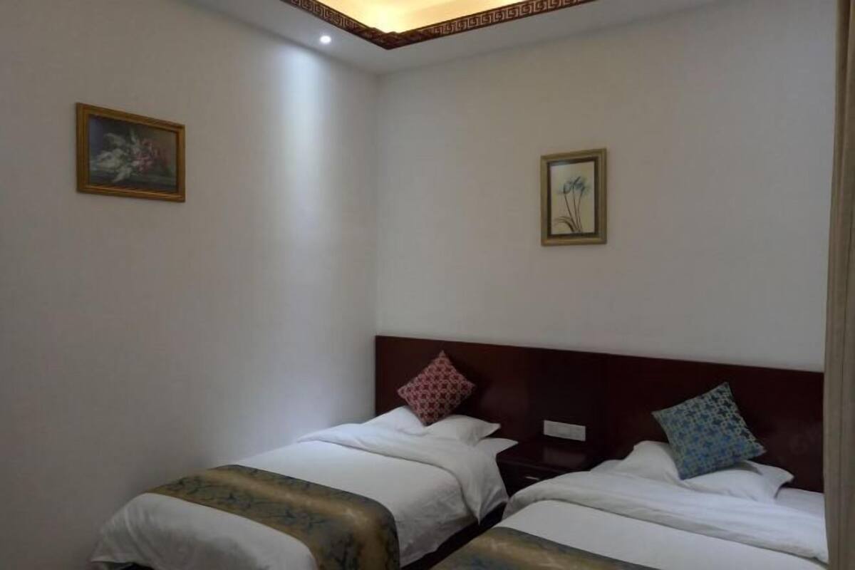 Quarto de hotel com duas camas, uma cabeceira de madeira e teto com padrão decorativo.