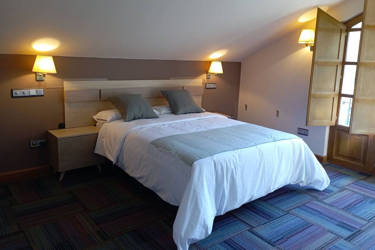 Quarto de hotel com uma cama grande, duas mesas de cabeceira e duas luminárias fixadas na parede.