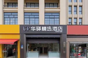 Entrada de hotel com placa em caracteres chineses, porta de vidro e fachada com toldo amarelo.