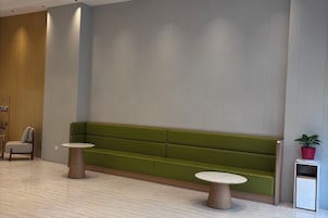 Uma área de recepção com um sofá verde, duas mesas redondas e um pequeno vaso de planta.