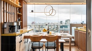 Uma cozinha moderna com vista para a cidade, com bancada de mármore, armários de madeira e um espaço de jantar com duas cadeiras e uma mesa posta para dois.