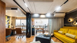 Uma sala de estar moderna com um sofá amarelo, um banquinho preto e uma área de jantar com vista para a cidade.