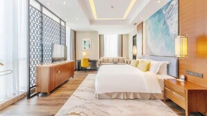 Quarto de hotel moderno com uma cama grande, cabeceira de madeira, mesa de cabeceira, televisão e uma janela ampla.