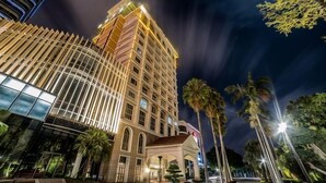 Um hotel com várias andares e fachada curva, com palmeiras e uma rua bem iluminada.