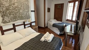 Quarto com uma cama grande, uma cama menor, uma escrivaninha e um candelabro.