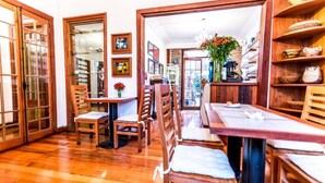 Uma área de refeições de madeira com uma mesa comprida e cadeiras, rodeada por prateleiras de madeira com diversos objetos.
