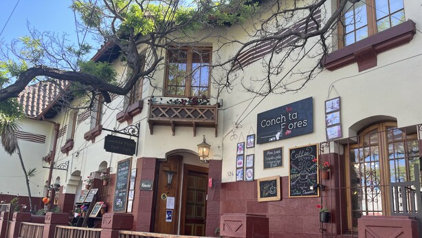 Um café com uma placa que diz “Conchita Flores B&B – Café” e um quadro de cardápio.