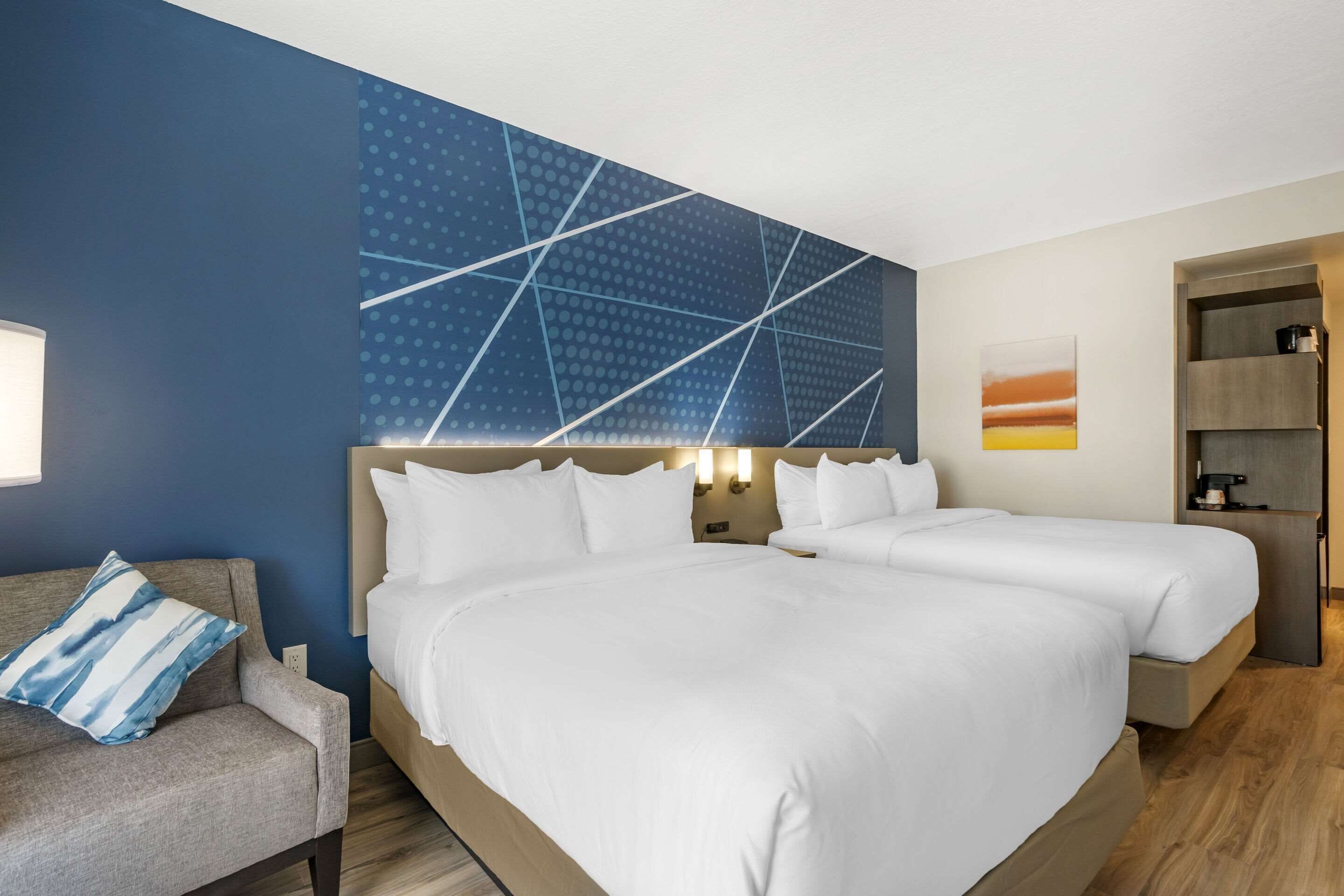 Quarto de hotel com duas camas, um sofá, uma parede com padrão geométrico e um quadro.