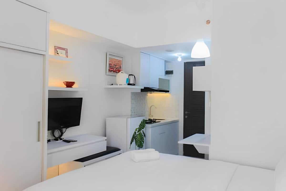 Quarto compacto e moderno, com uma cama, pequeno espaço de cozinha e televisão.