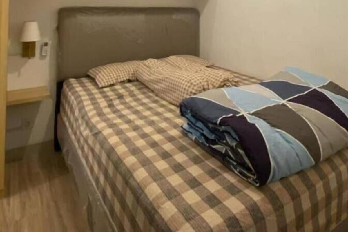 Quarto com cama, cabeceira, prateleira na parede e aparelho de ar condicionado.