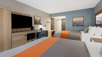 Quarto de hotel com uma cama grande, uma escrivaninha com computador, televisão e um quadro na parede.
