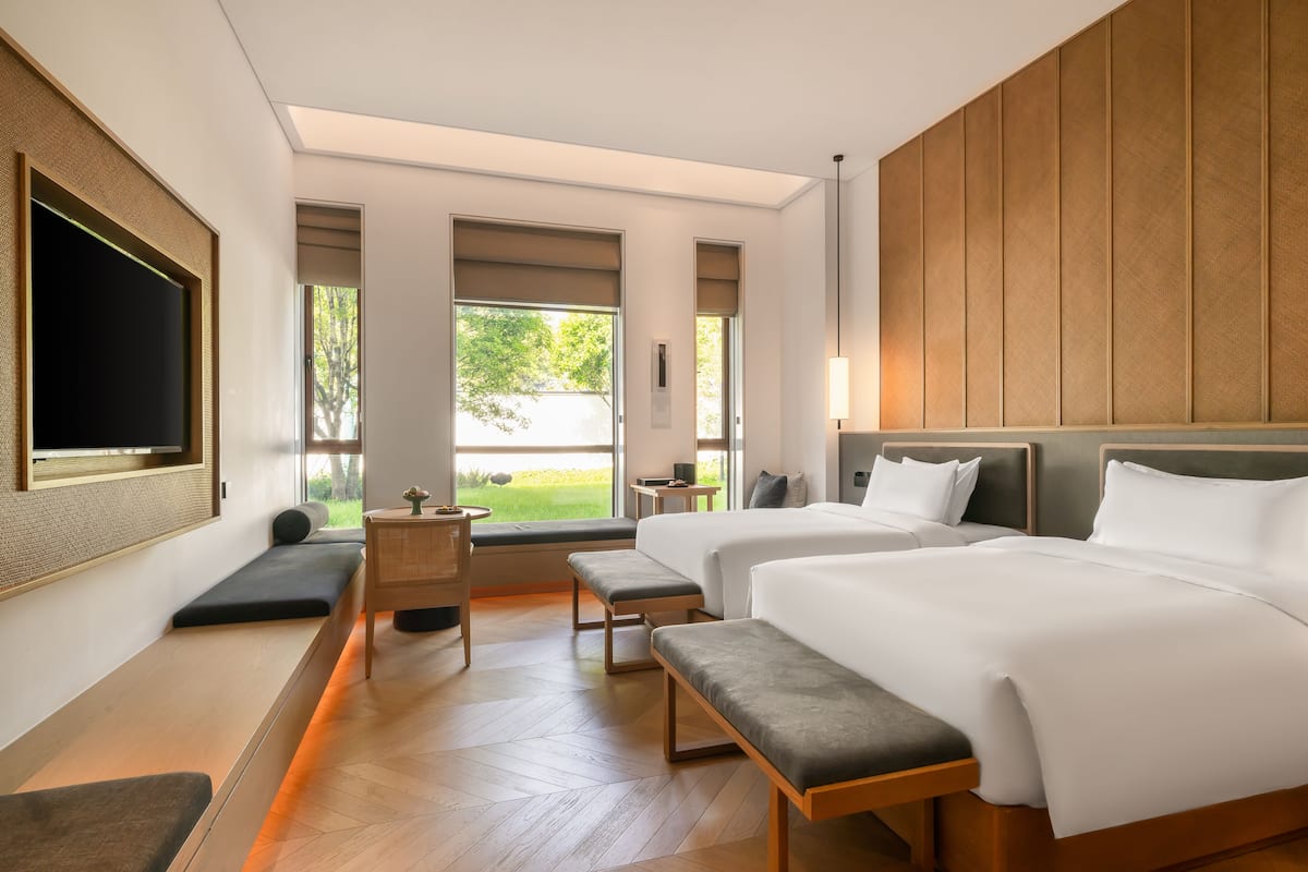 Quarto de hotel moderno com duas camas, um banco, uma escrivaninha e uma televisão.