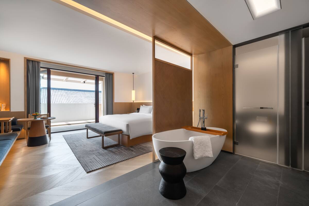 Quarto de hotel moderno com uma cama grande, banheira, escrivaninha e vista para o exterior.