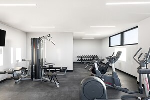 Uma academia com diversos equipamentos de exercício, incluindo esteiras e aparelhos de musculação, além de um suporte com halteres.