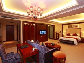 Quarto de hotel com cama, televisão, escrivaninha e área de estar.