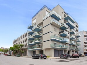 Um edifício residencial com vários andares, varandas, área de estacionamento e céu claro.
