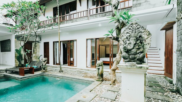 Área de piscina com uma estátua, uma espreguiçadeira e uma escadaria que dá para uma varanda.