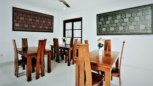 Uma sala de jantar com mesa e cadeiras de madeira, um ventilador de teto e dois grandes painéis de parede estampados.