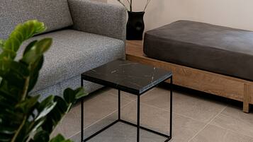 Uma sala de estar moderna com um sofá cinzento, um banco de madeira, uma mesa de centro preta e um vaso com flores.