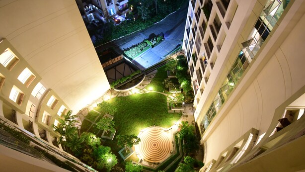 Vista aérea de um pátio de hotel com um jardim circular central, edifícios ao redor e um caminho.