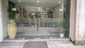Entrada de um hotel com porta de vidro e placa com a inscrição "THE XEN SUITES".