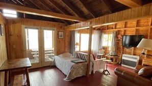 Interior acolhedor de uma cabana com uma cama, um sofá, uma televisão e um espaço de jantar.