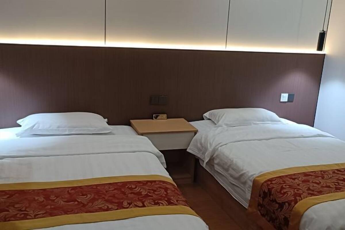 Quarto de hotel com duas camas, uma mesinha de cabeceira e cabeceira de madeira.
