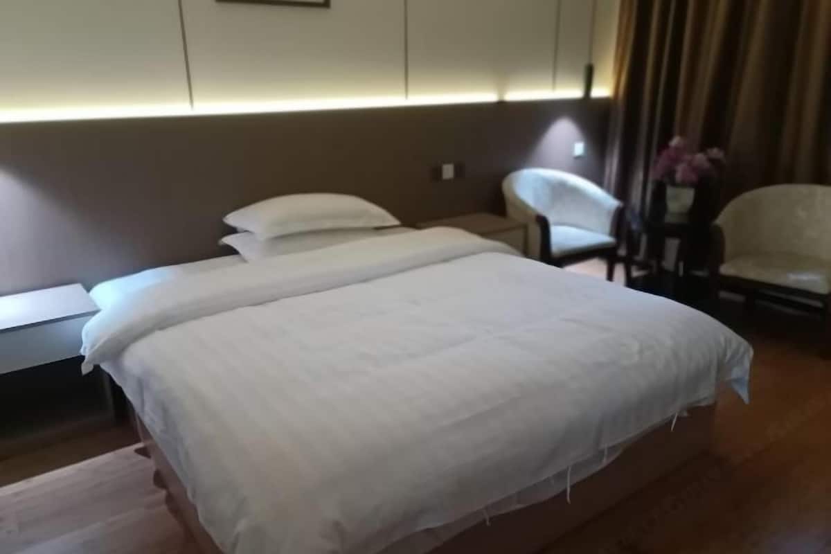 Quarto de hotel com cama grande, duas almofadas brancas, mesa de cabeceira e uma cadeira.