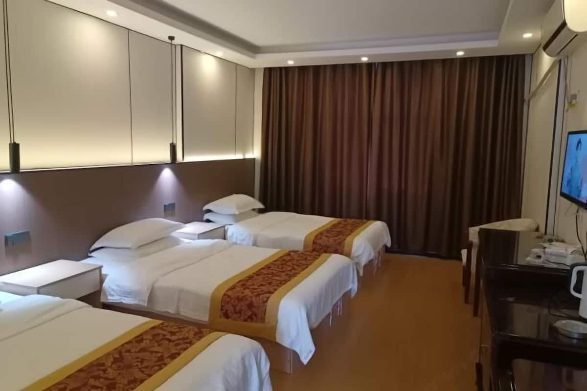 Quarto de hotel com três camas, uma escrivaninha, televisão e uma janela grande com cortinas.