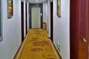 Um corredor com carpete estampado, portas de ambos os lados e um interruptor de luz na parede.