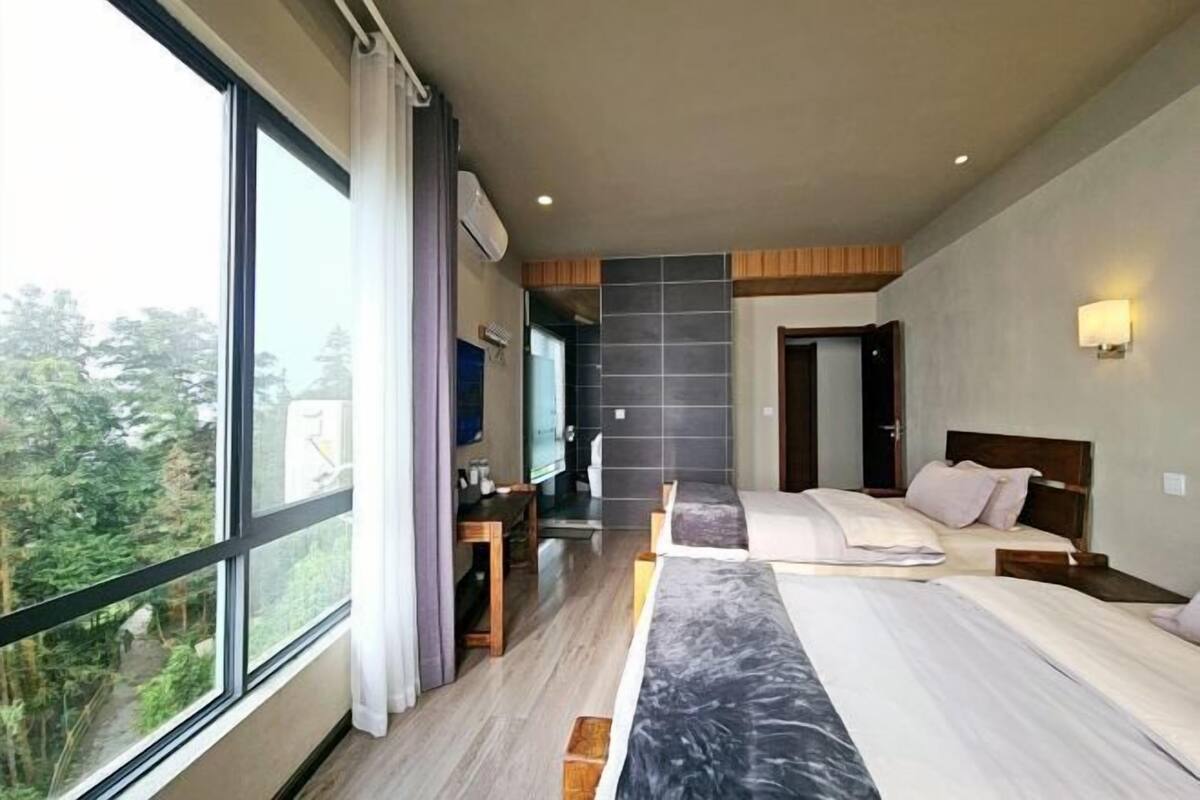 Quarto de hotel moderno com uma janela grande, uma cama, uma escrivaninha e uma televisão.