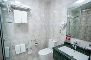 Casa de banho com cabine de duche em vidro, sanita, lavatório com bancada em mármore verde e espelho.