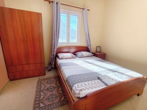 Quarto com cama de madeira, mesa de cabeceira, guarda-roupa e janela com cortinas.