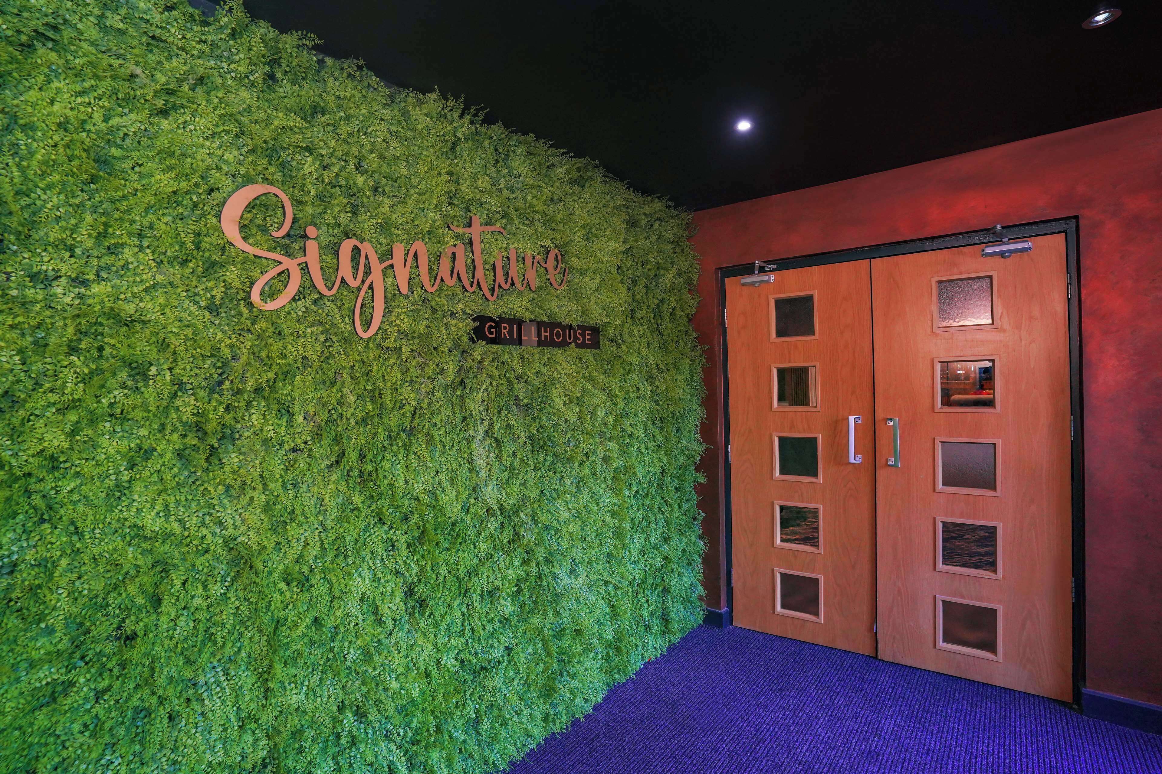 Pared com uma placa 'Signature GRILLHOUSE' e um conjunto de portas de madeira duplas.