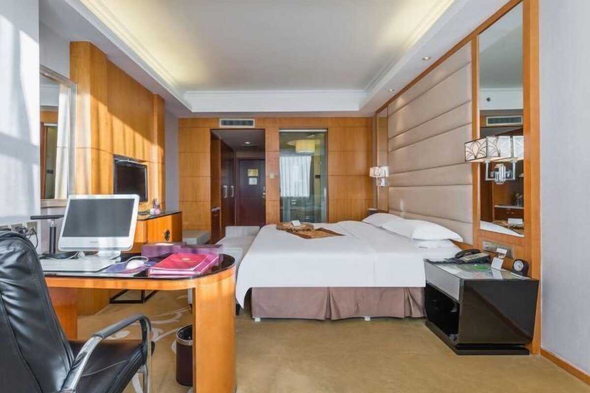 Quarto de hotel com cama, escrivaninha, computador, cadeira e um espelho grande.