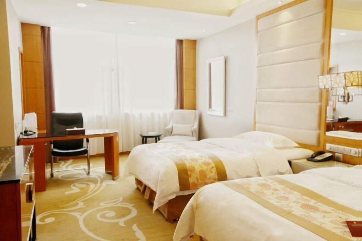 Quarto de hotel com duas camas, uma mesa, uma cadeira e uma mesa de cabeceira com abajur.