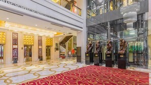 Um saguão de hotel com carpete vermelho, escadaria e fachada de vidro.