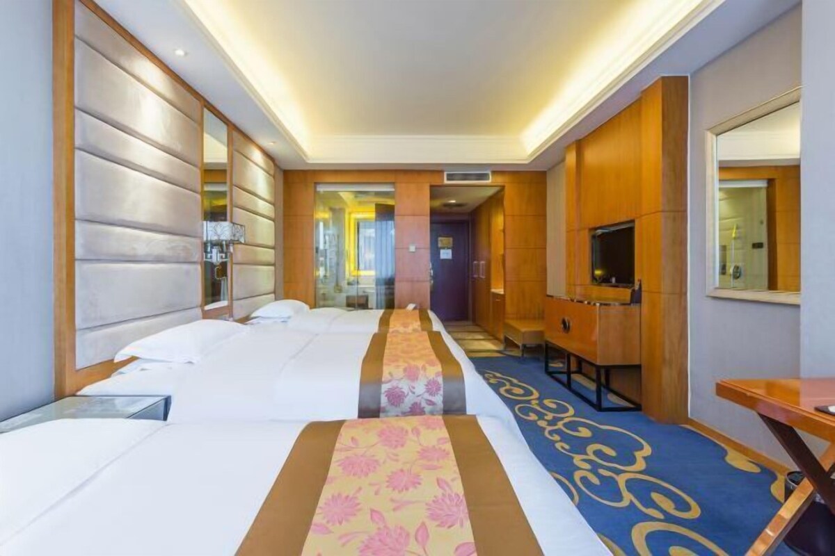 Quarto de hotel com duas camas, televisão, secretária e casa de banho visível pela porta.