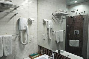 Casa de banho com paredes revestidas a azulejos brancos, zona de duche e lavatório com espelho.