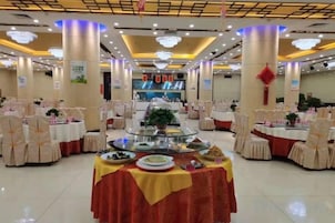 Salão de festas com mesas redondas, cadeiras e um detalhe decorativo central.